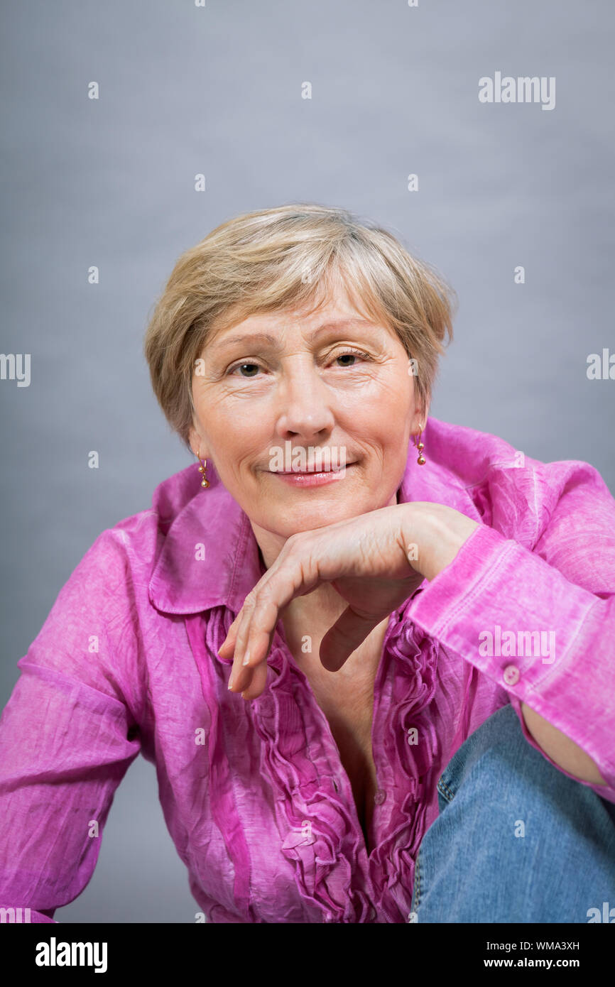 Beautiful blond trendy senior woman posing in a pink blouse and jeans ...