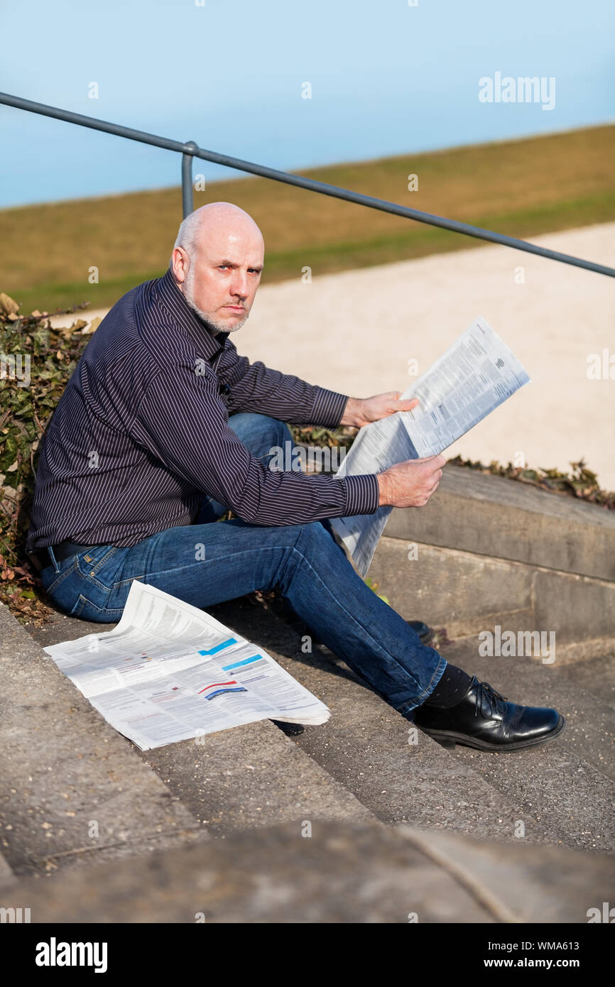 Man sitting on steps reading a newspaper Stock Photo - Alamy