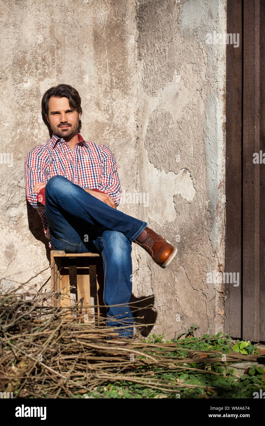 Smiling male model sitting on wooden crate with legs crossed Stock ...