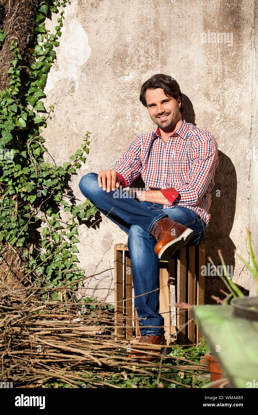 Smiling male model sitting on wooden crate with legs crossed Stock ...