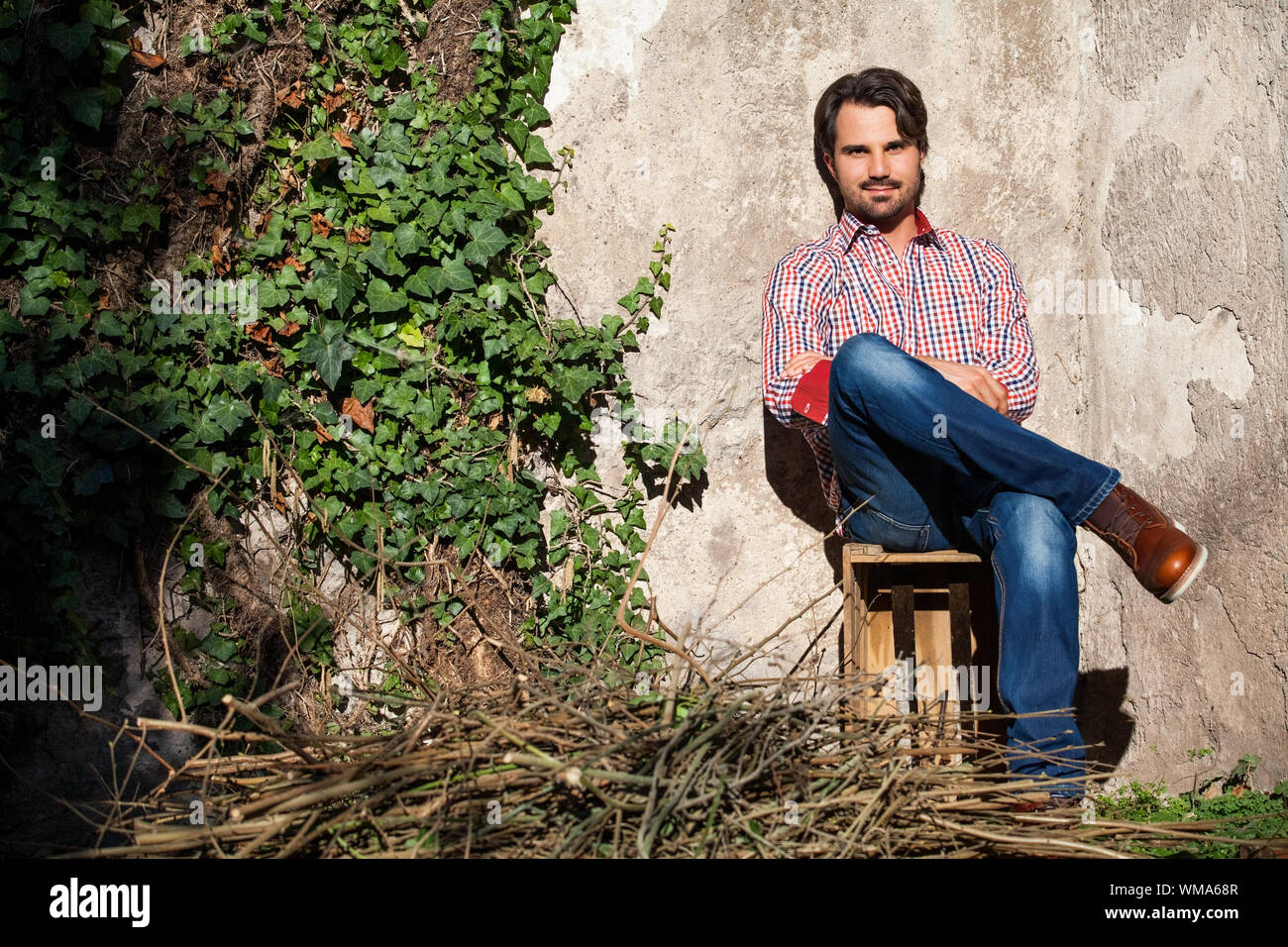 Smiling male model sitting on wooden crate with legs crossed Stock ...