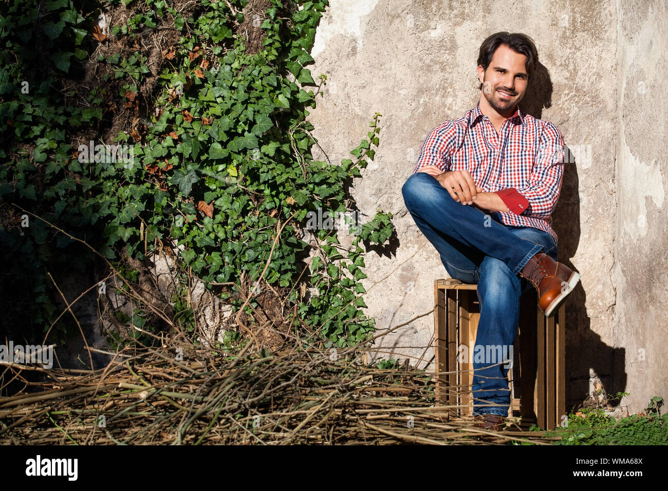 Smiling male model sitting on wooden crate with legs crossed Stock ...