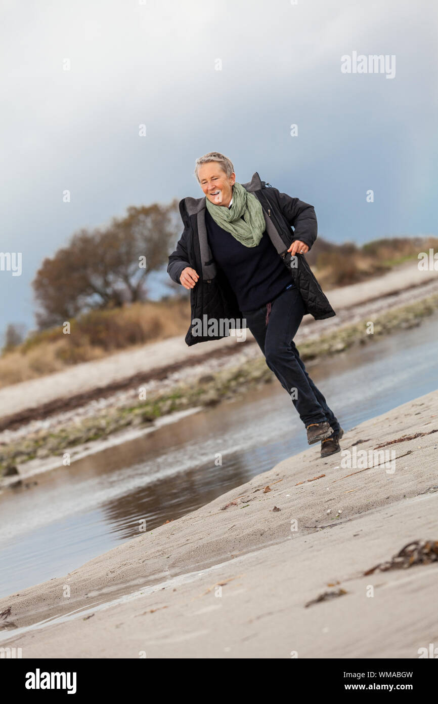 Happy senior woman frolicking on the beach striding along with ...