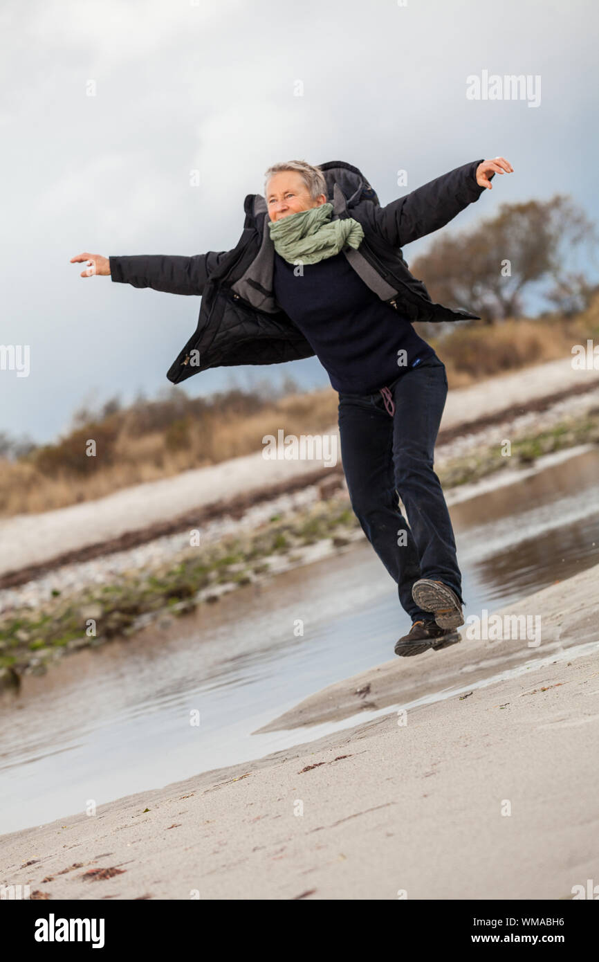 Happy senior woman frolicking on the beach striding along with ...