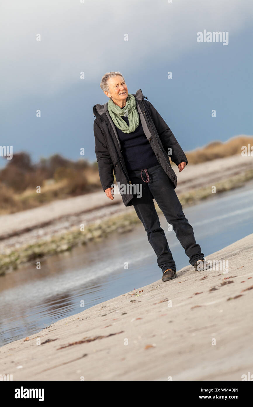 Happy senior woman frolicking on the beach striding along with ...