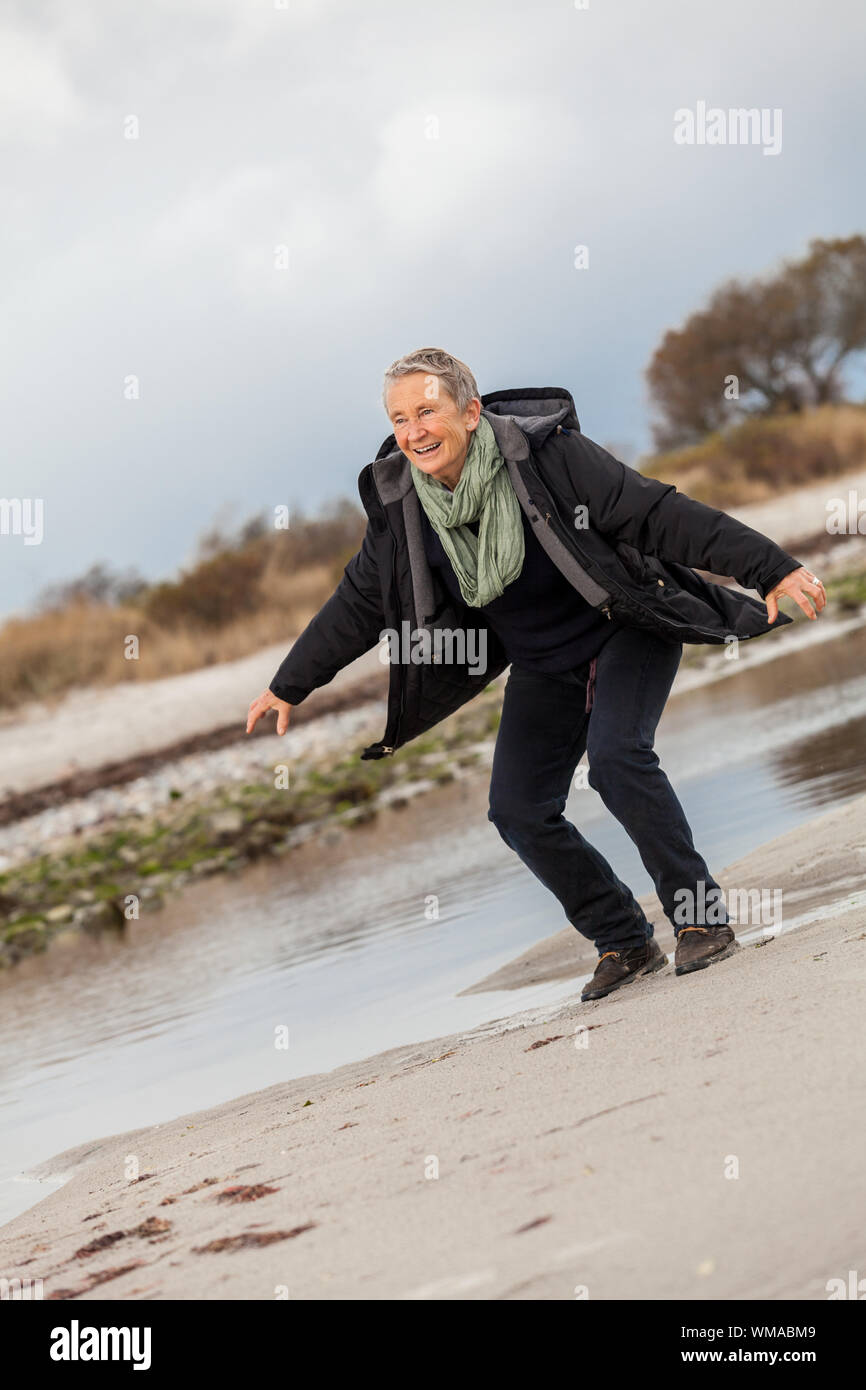 Happy senior woman frolicking on the beach striding along with ...