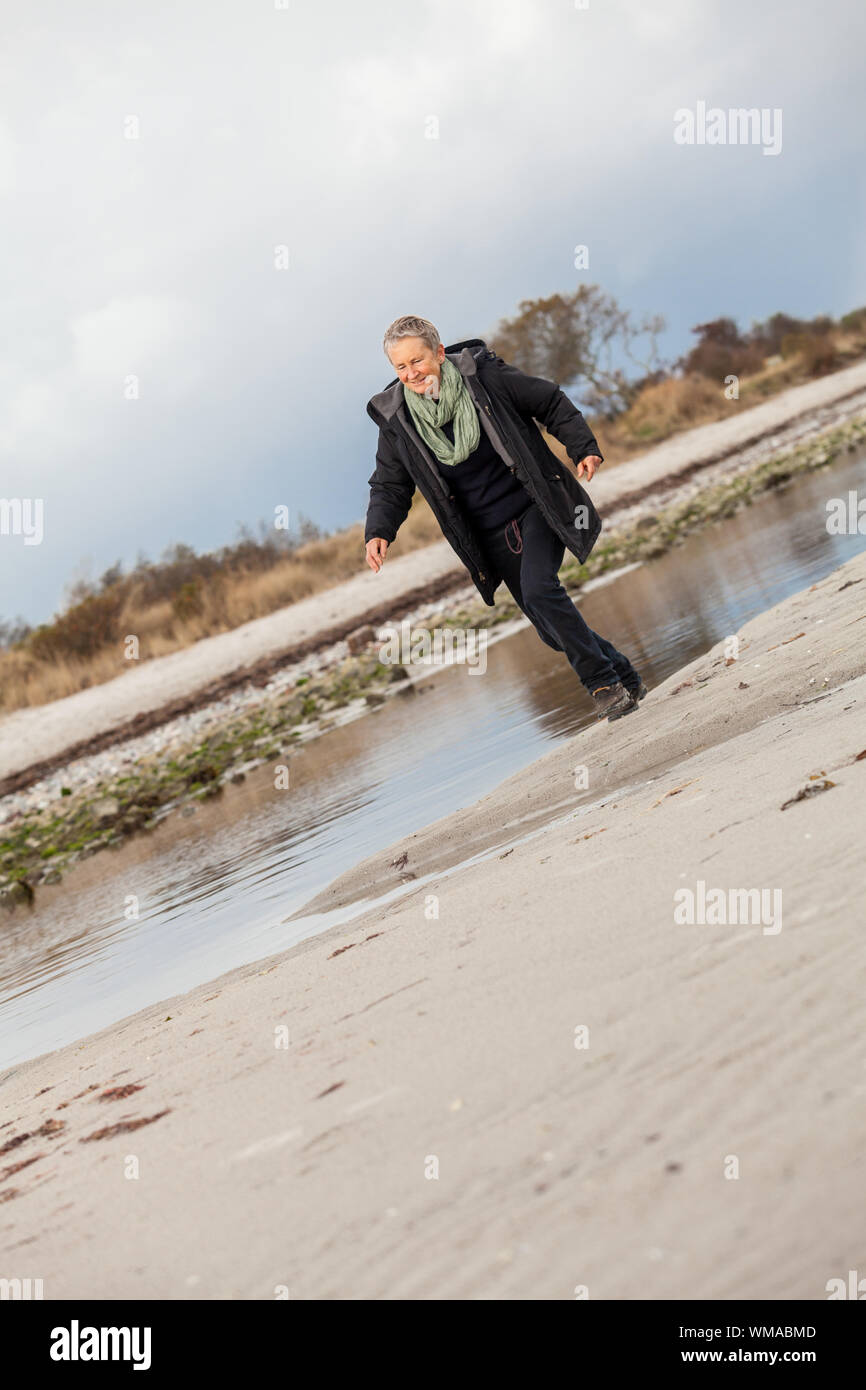Happy senior woman frolicking on the beach striding along with ...