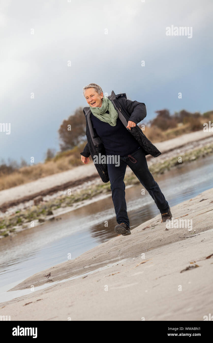 Happy senior woman frolicking on the beach striding along with ...