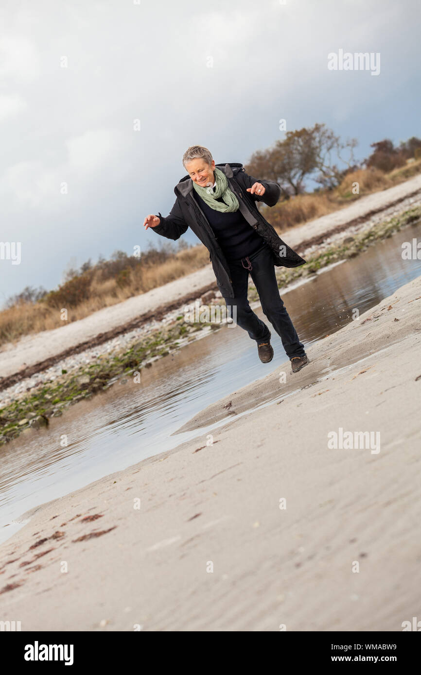 Happy senior woman frolicking on the beach striding along with ...