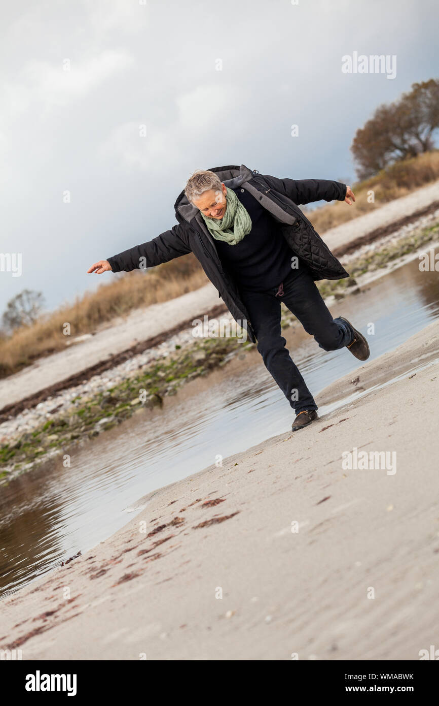Happy senior woman frolicking on the beach striding along with ...