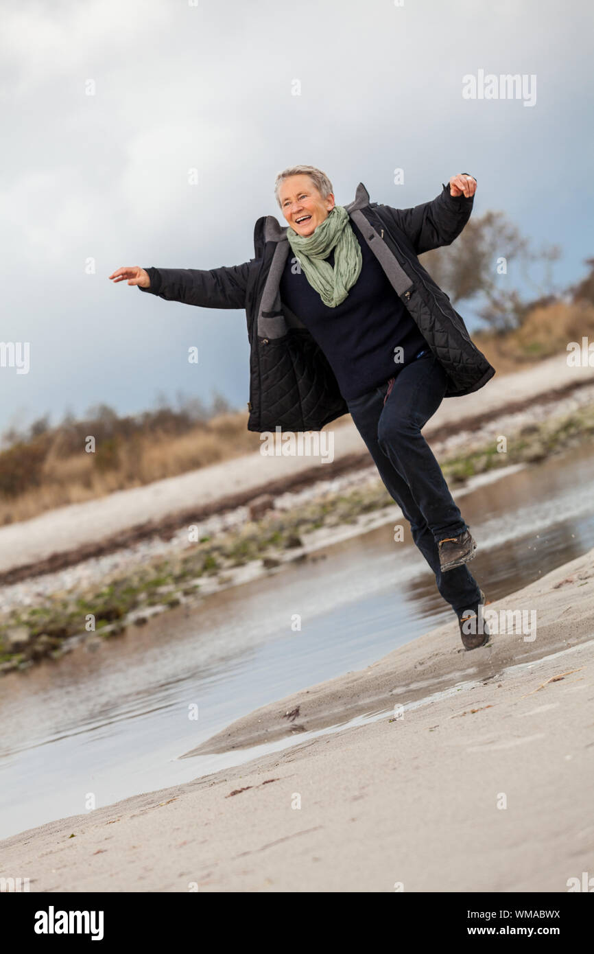 Happy senior woman frolicking on the beach striding along with ...