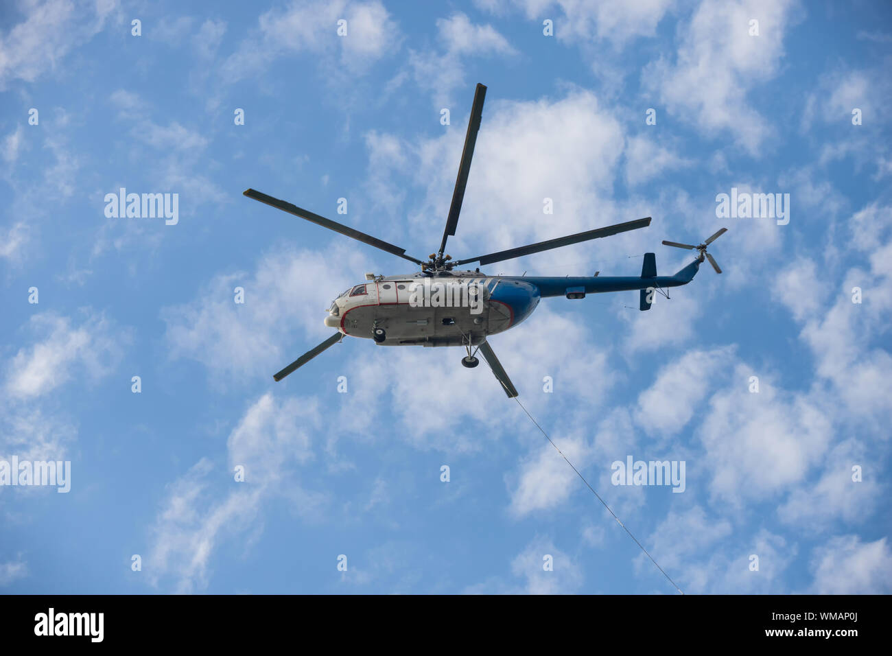 A white and blue helicopter flying in the sky - the cable hangs out of ...