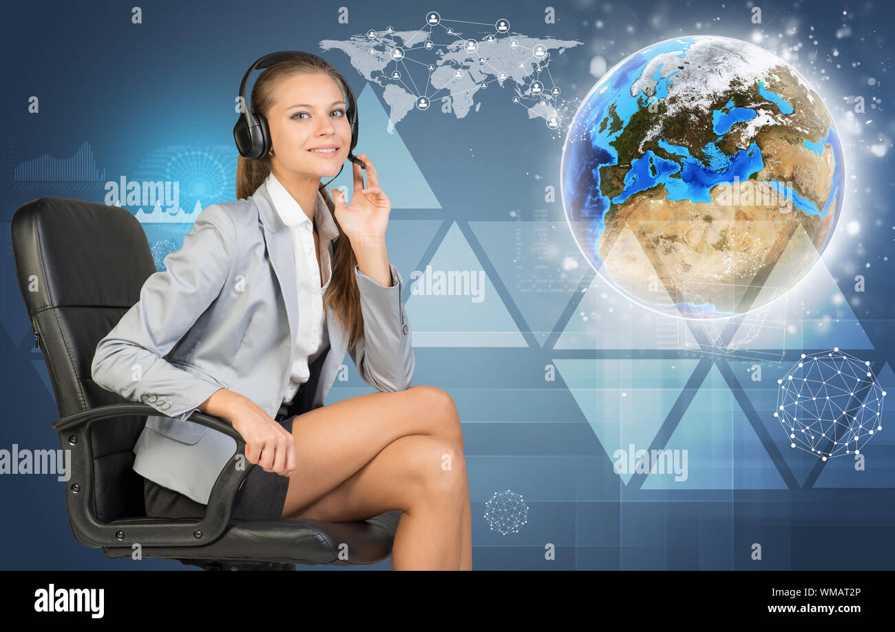 Businesswoman in headset, sitting on office chair, her hand on microphone, looking at camera ...