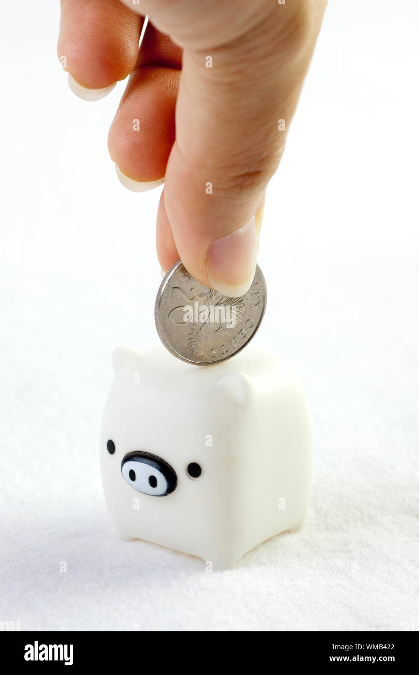 Hand inserting coin to a small piggy bank Stock Photo - Alamy