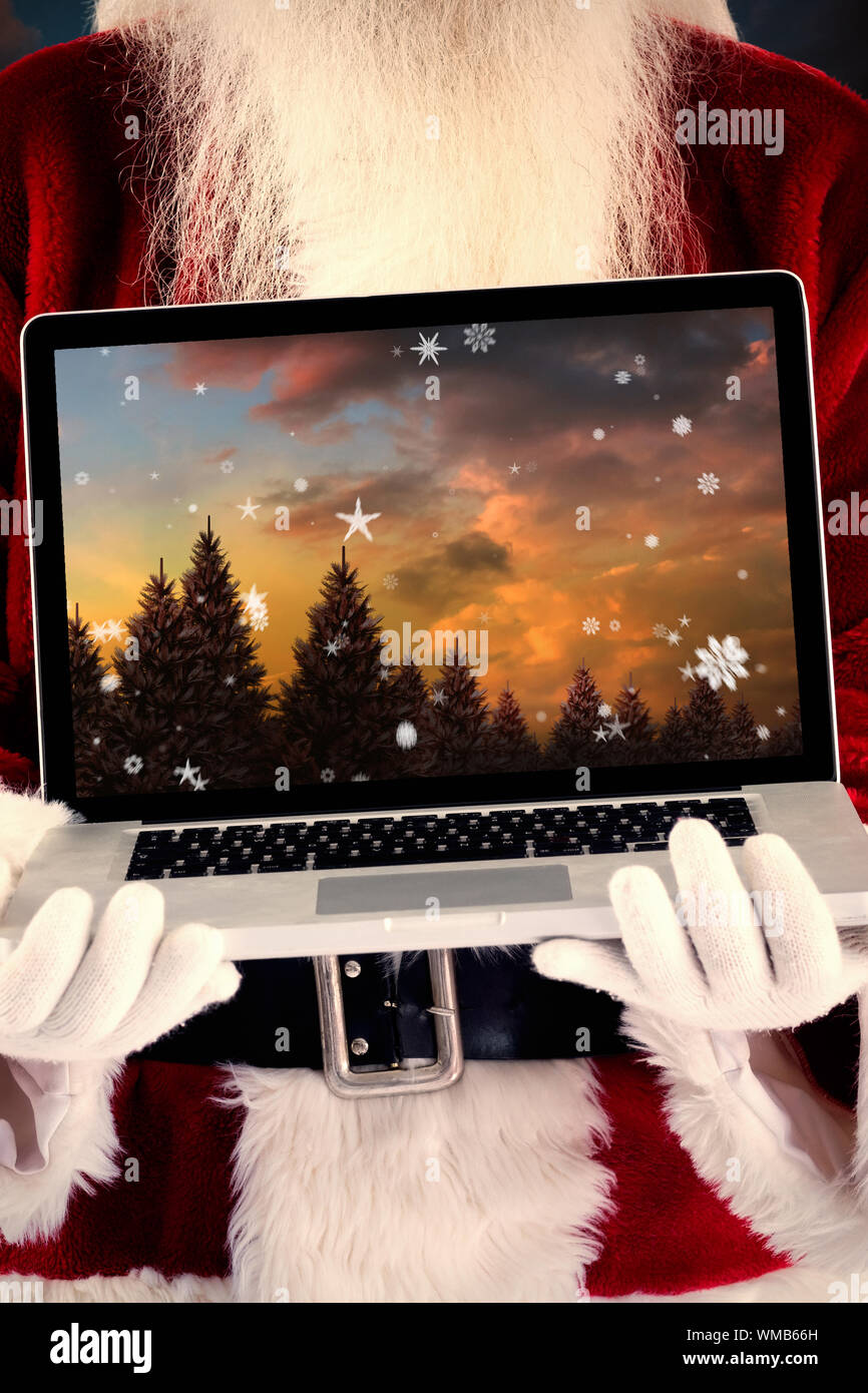 Santa Claus presents a laptop against snowy landscape with fir trees ...