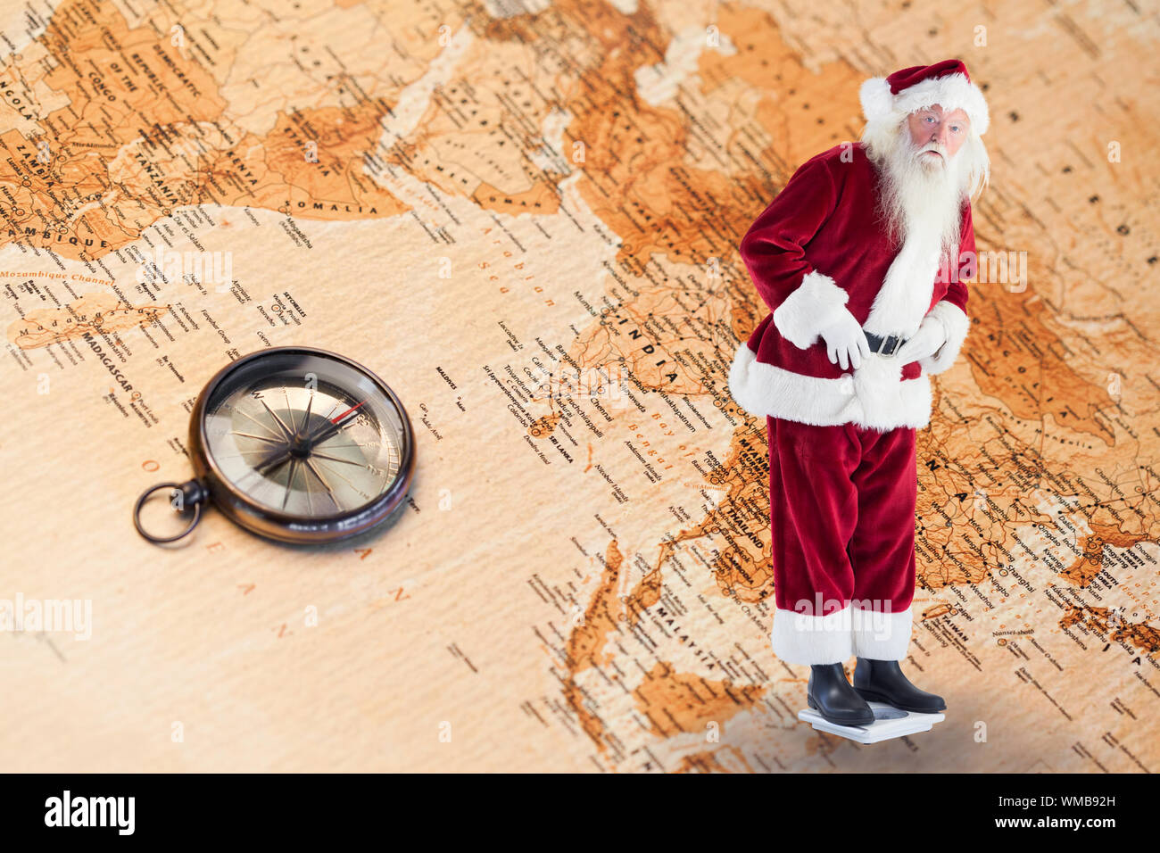 Santa is surprised about his weight against world map with compass ...
