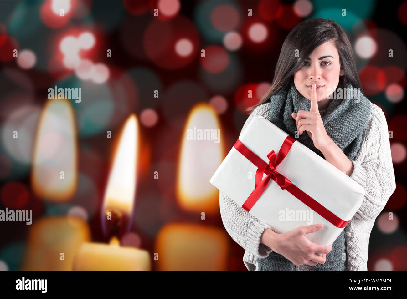 Brunette holding gift and keeping a secret against candle burning ...