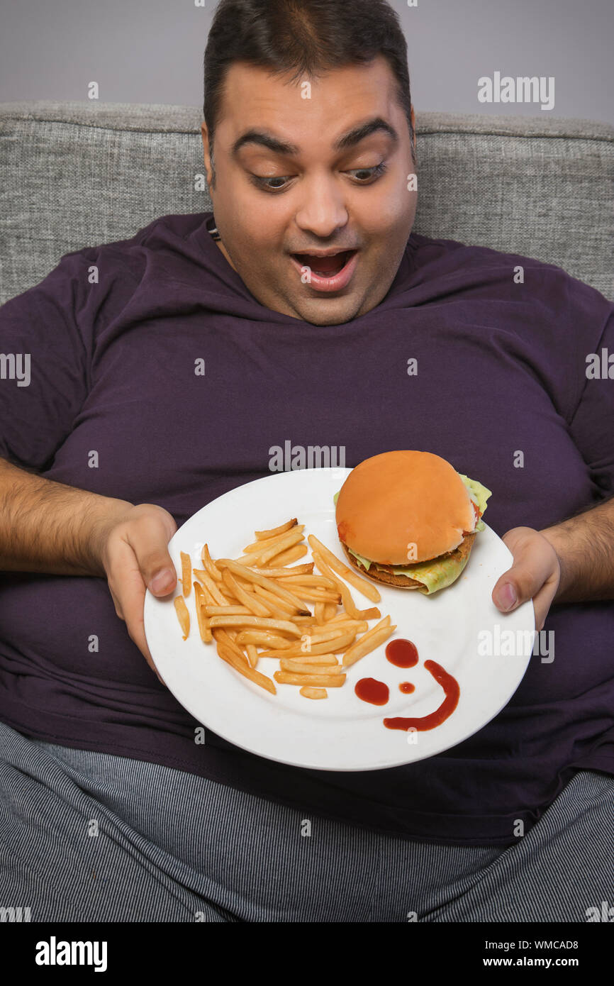 Happy obese man holding a plate with burger and french fries with a ...