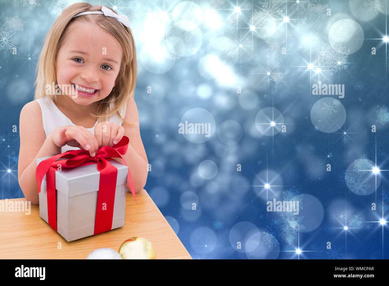 Festive little girl opening a gift against shimmering light design on ...