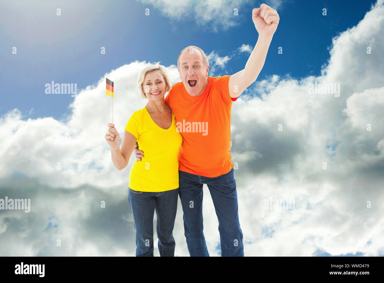Happy german couple cheering at camera against blue sky with clouds ...