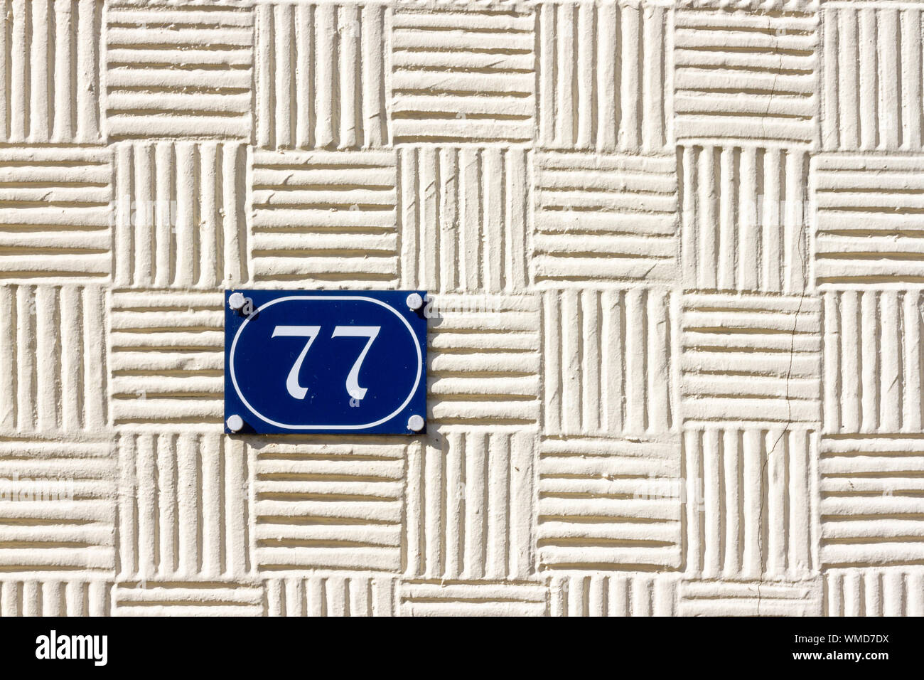 House number 77 on a structured plaster wall with square pattern of ...