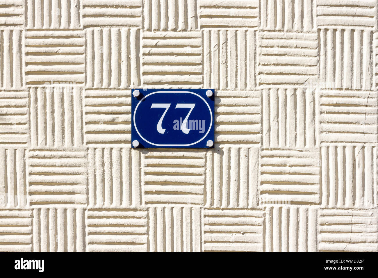 House number 77 on a structured plaster wall with square pattern of ...