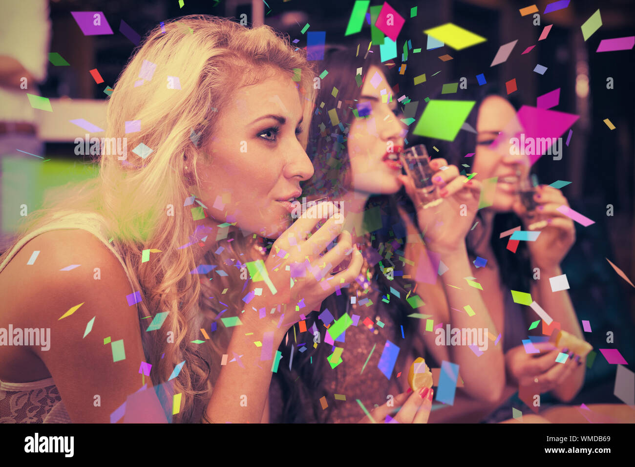 Happy friends drinking shots together against flying colours Stock ...