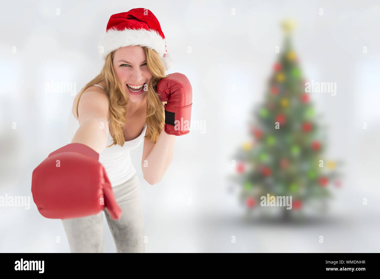 Festive blonde punching with boxing gloves against blurry christmas ...