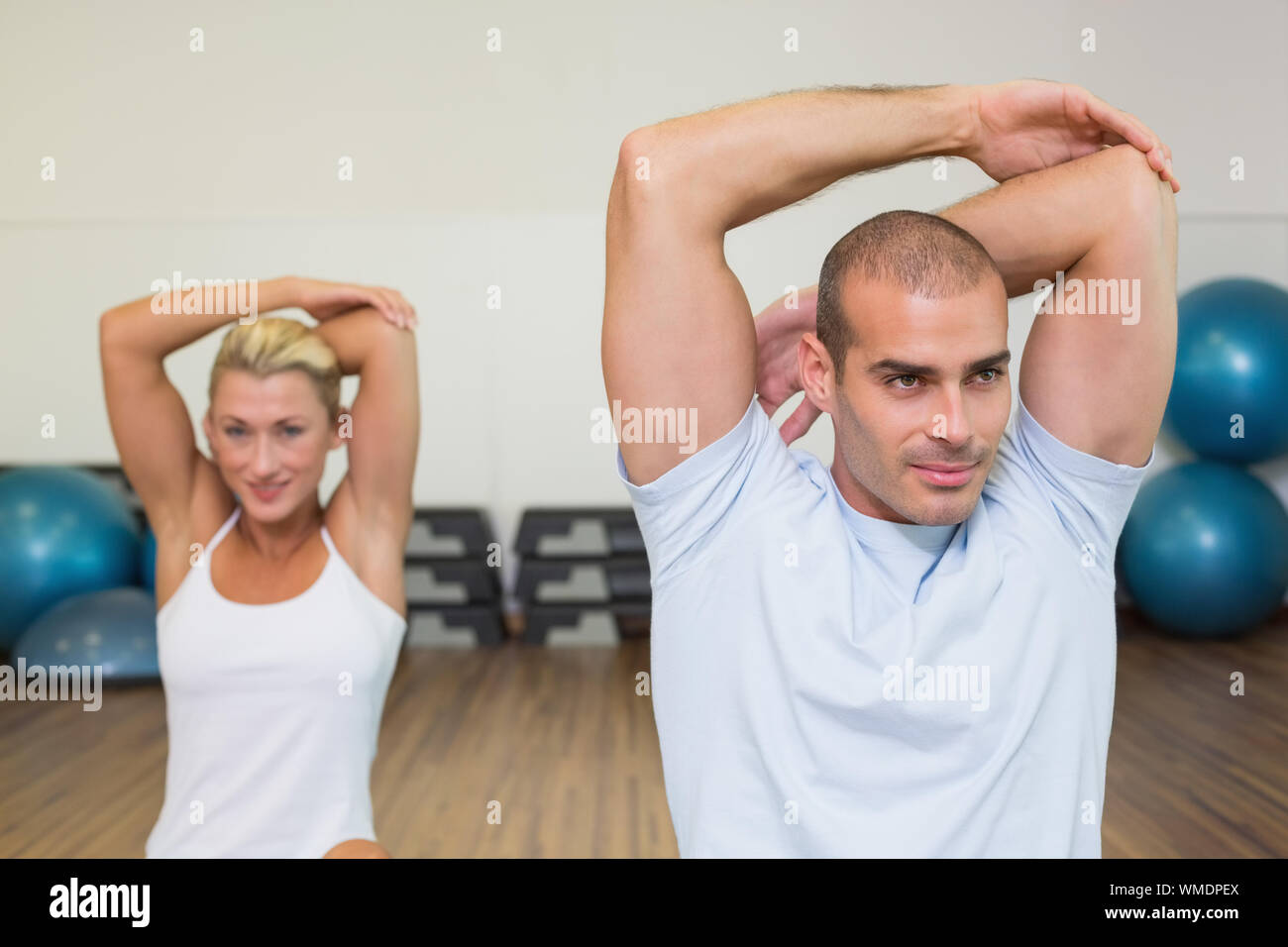 Portrait of young couple stretching hands behind back in yoga class ...