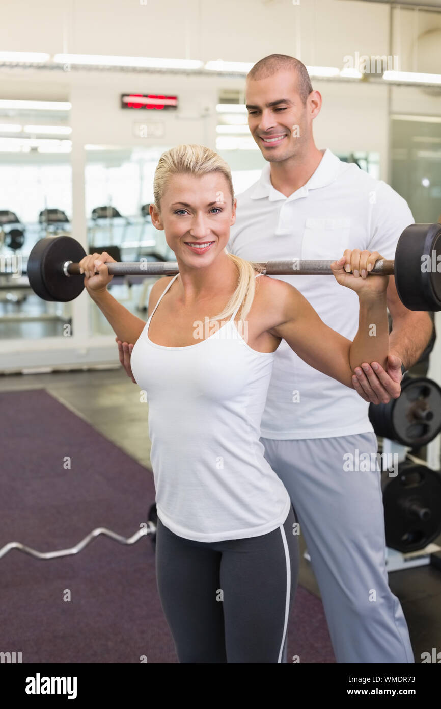 Personal male trainer helping young woman with lifting barbell in the ...