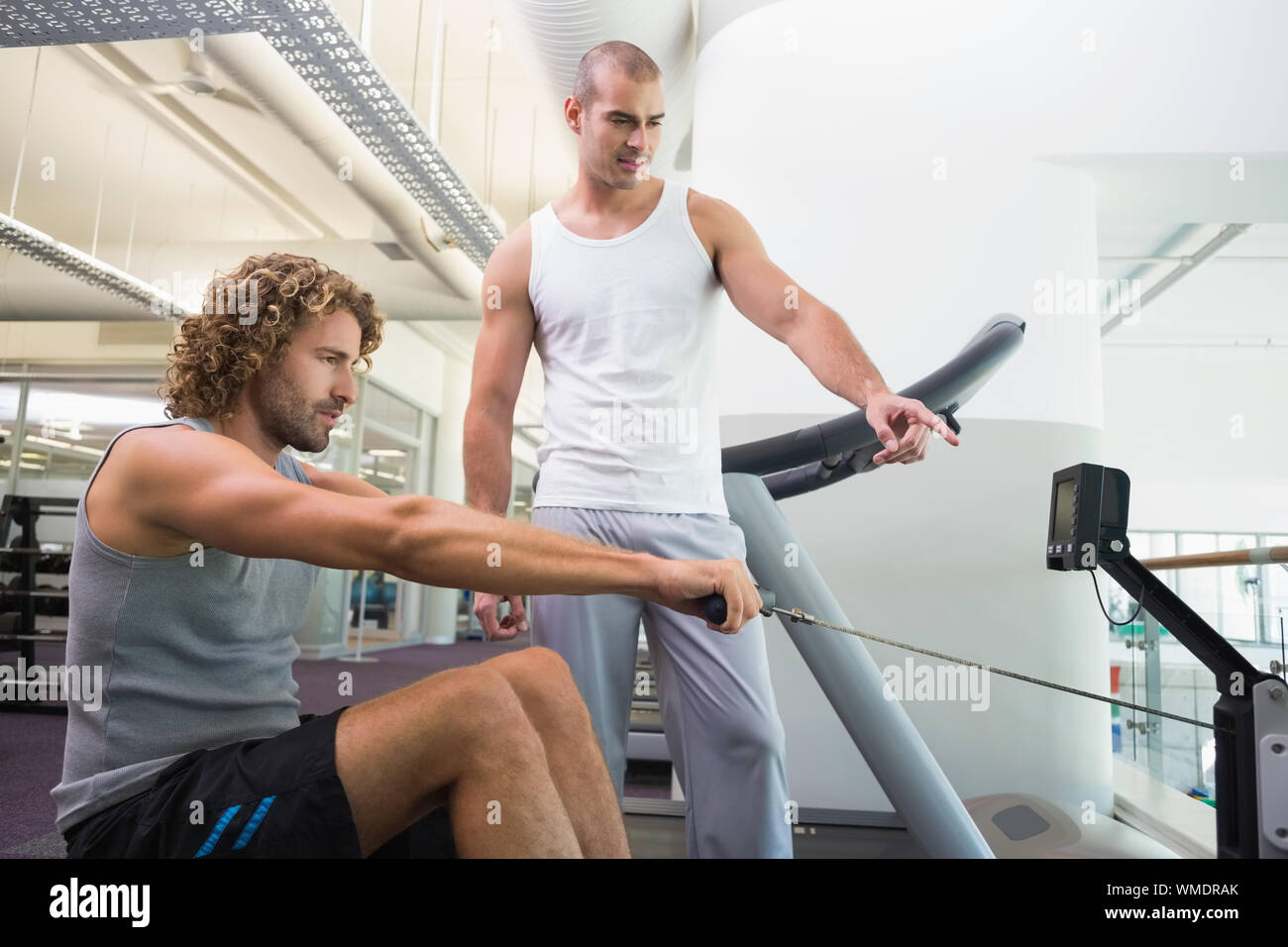 Side view of a male trainer assisting young man on fitness machine at ...