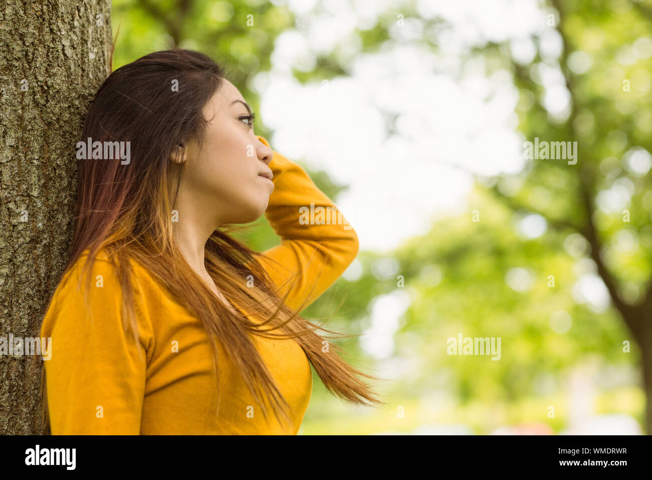Beautiful young woman standing against tree in the park Stock Photo - Alamy