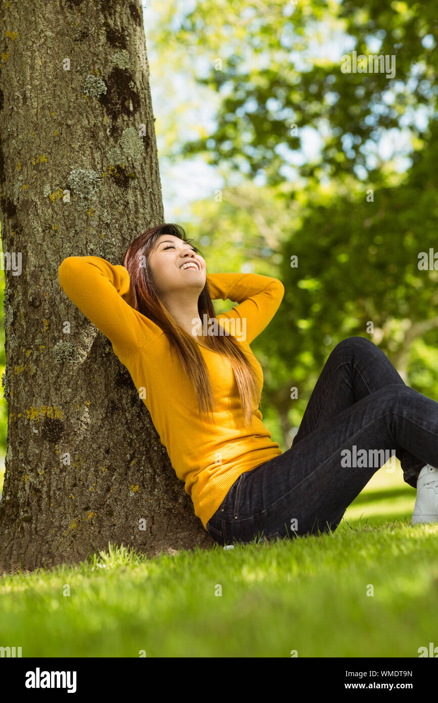 Side view of beautiful young woman sitting against tree in the park ...