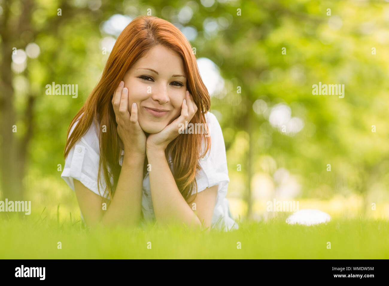 Portrait of a pretty redhead content and lying on grass Stock Photo - Alamy