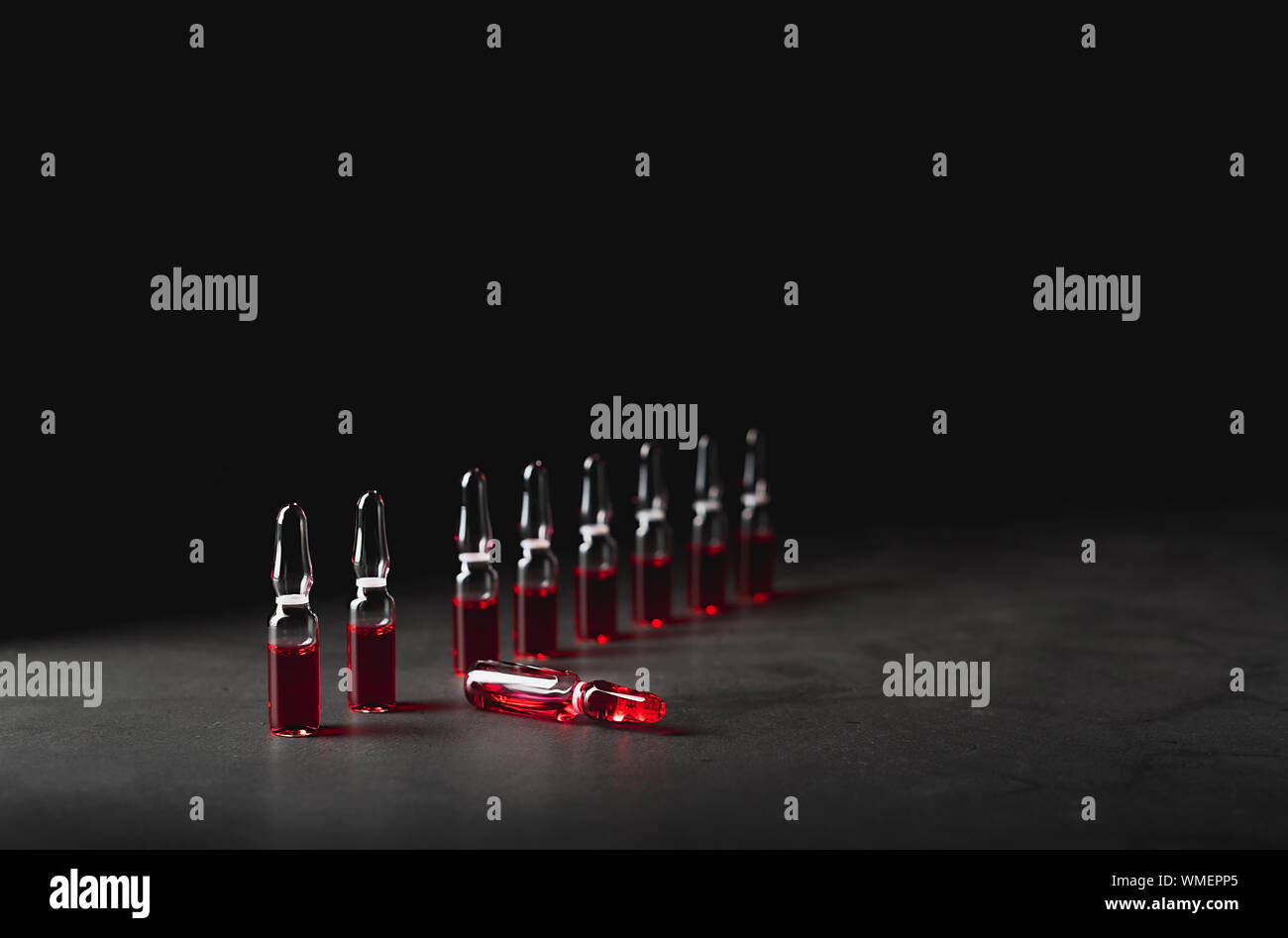 Row of ampules for injections with red liquid on dark background ...