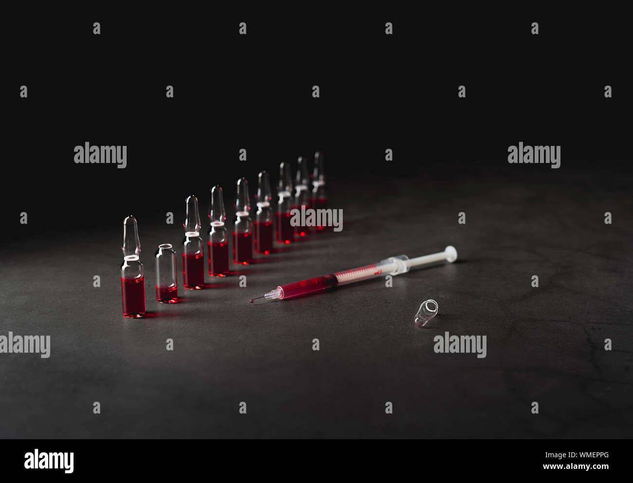 Syringe filled with red liquid from broken ampule on dark background ...