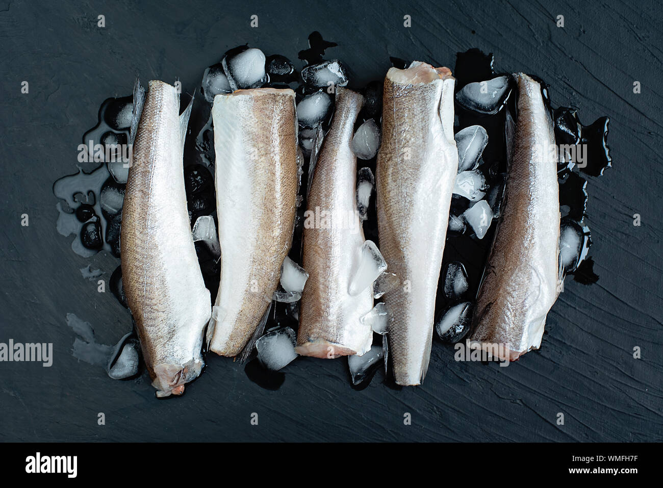 Raw fish hake. Five Raw fish fillet on ice on dark background, food ...