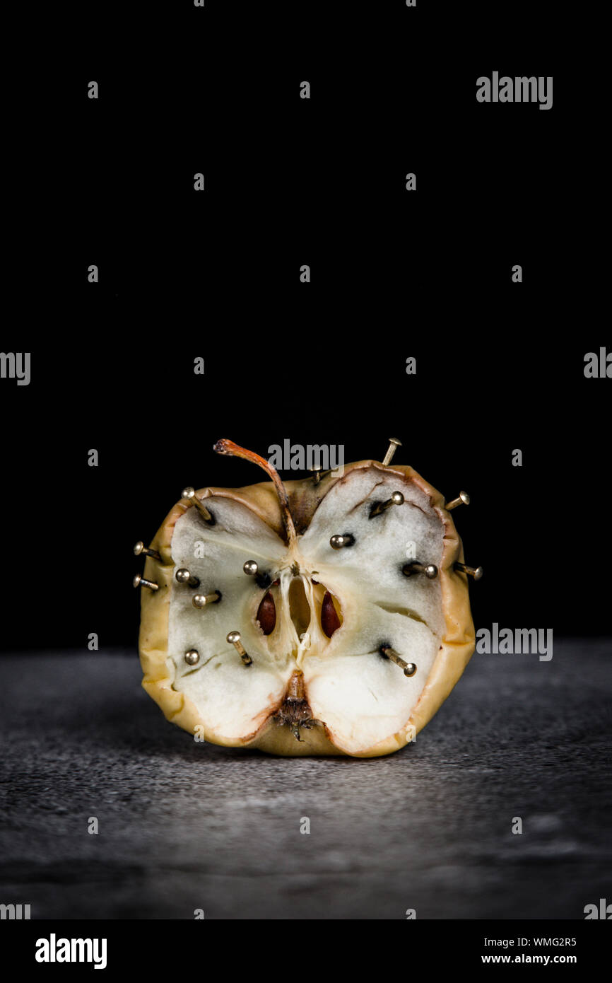 Dark photo of an apple stabbed with the screws Stock Photo - Alamy