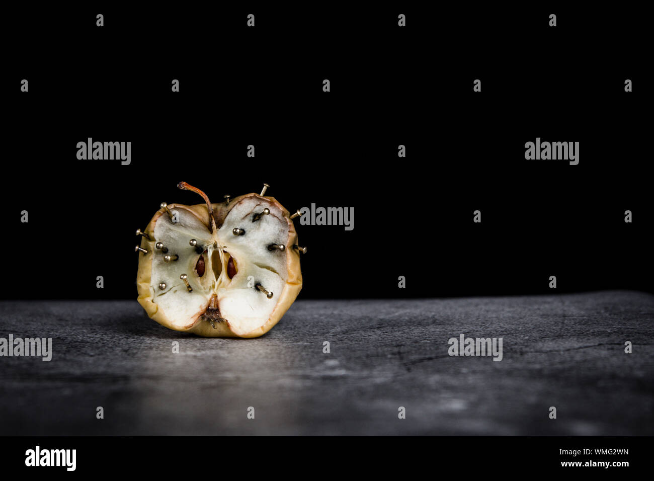 Dark photo of an apple stabbed with the screws Stock Photo - Alamy