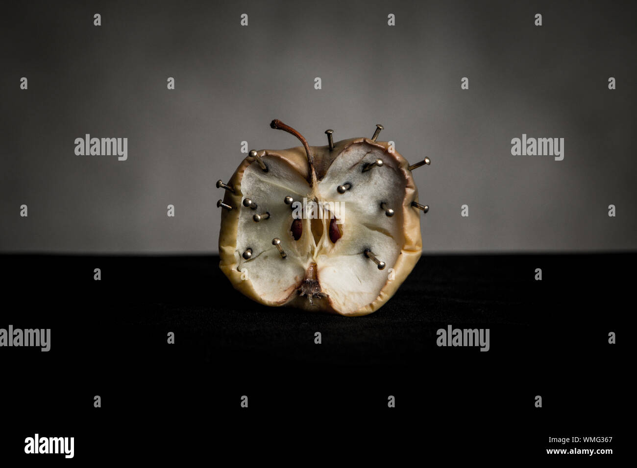 Dark photo of an apple stabbed with the screws Stock Photo - Alamy