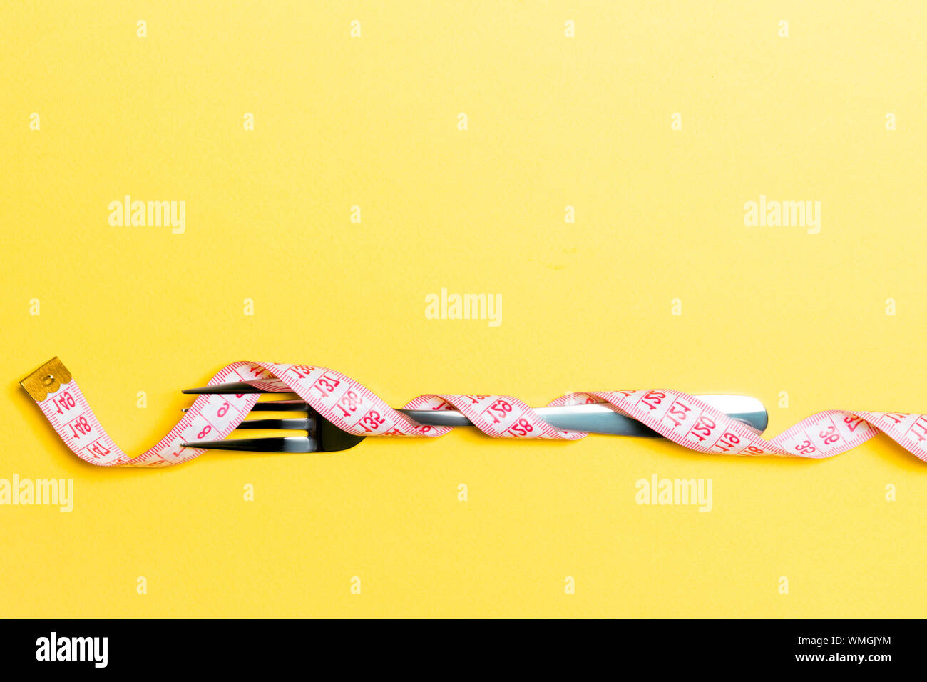 Composition of curled wrapped measuring tape and fork on yellow ...