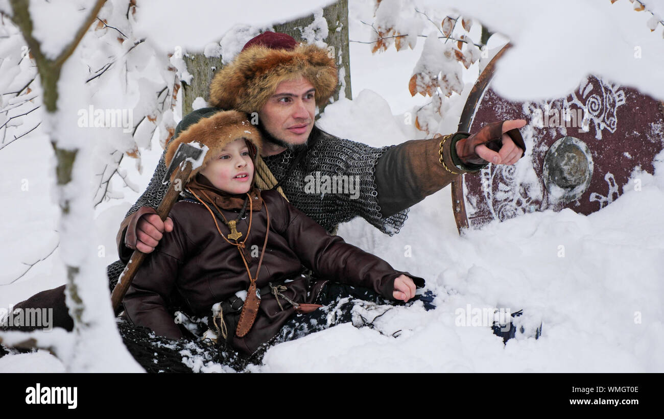 Father viking and his son sits and talking on the snow in the winter ...