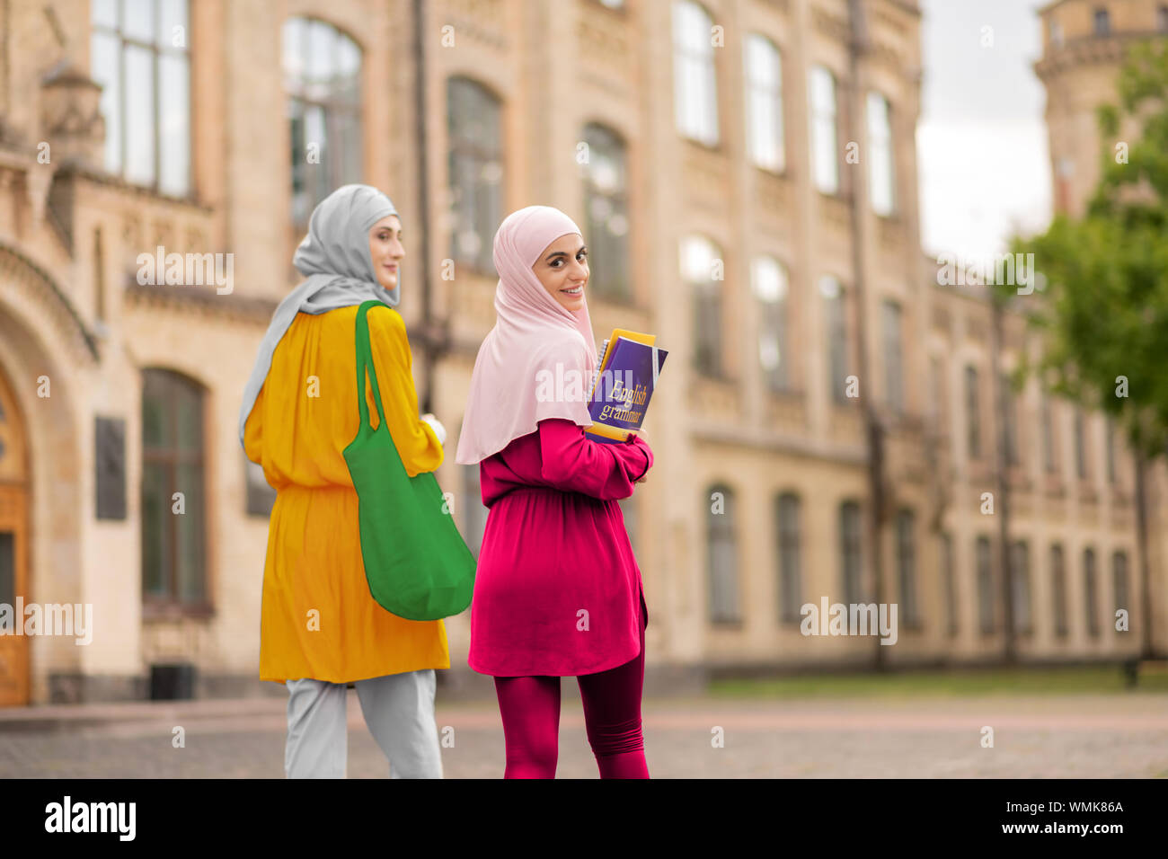Muslim student holding books walking to classes with friend Stock Photo ...