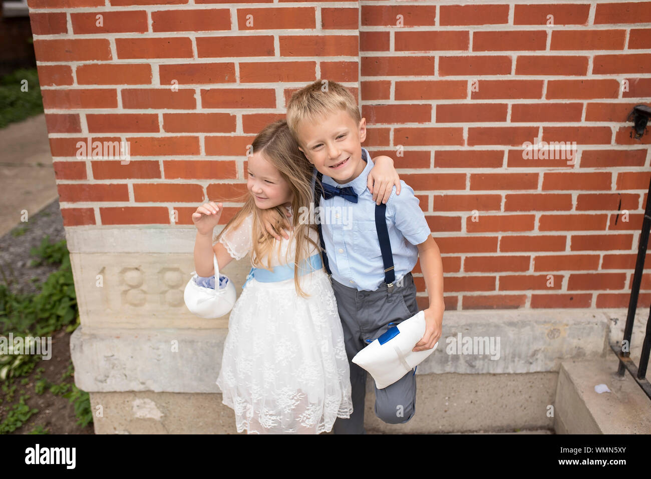 Flower girl and ring bearer stand against brick wall hugging Stock ...
