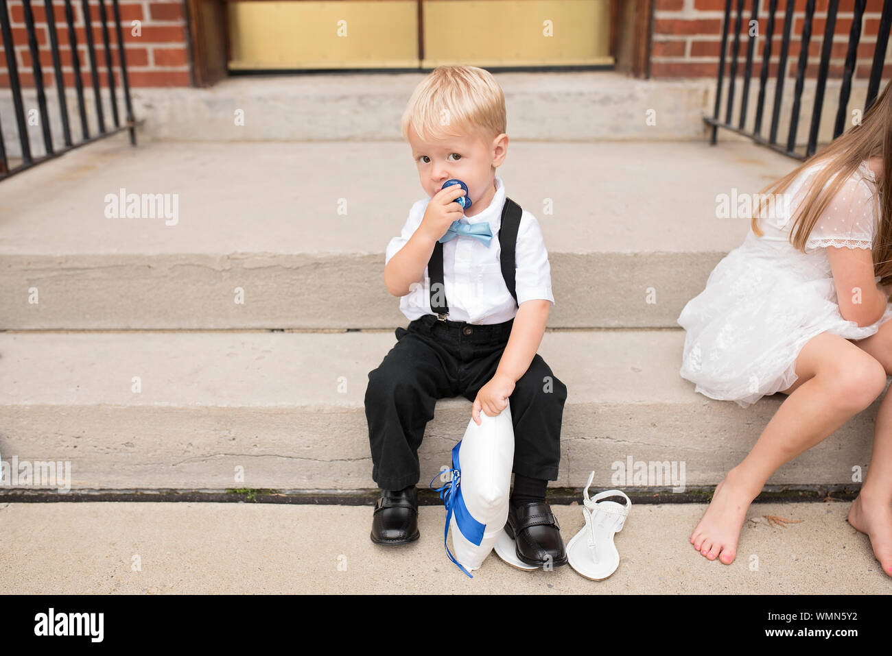 Ring bearer baby sits next to flower girl on steps and looks at camera ...
