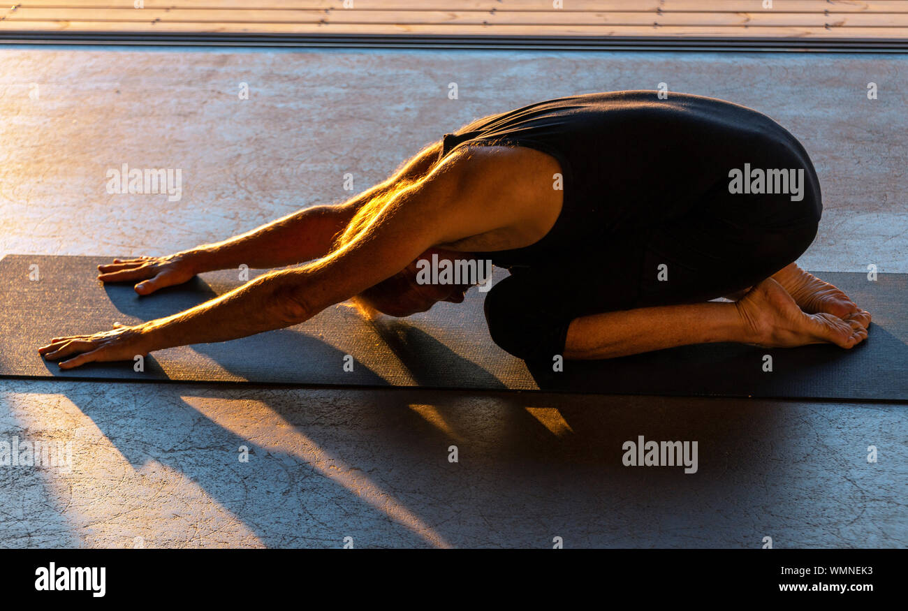 The orange light of sunset backlights a man performing a yoga pose ...
