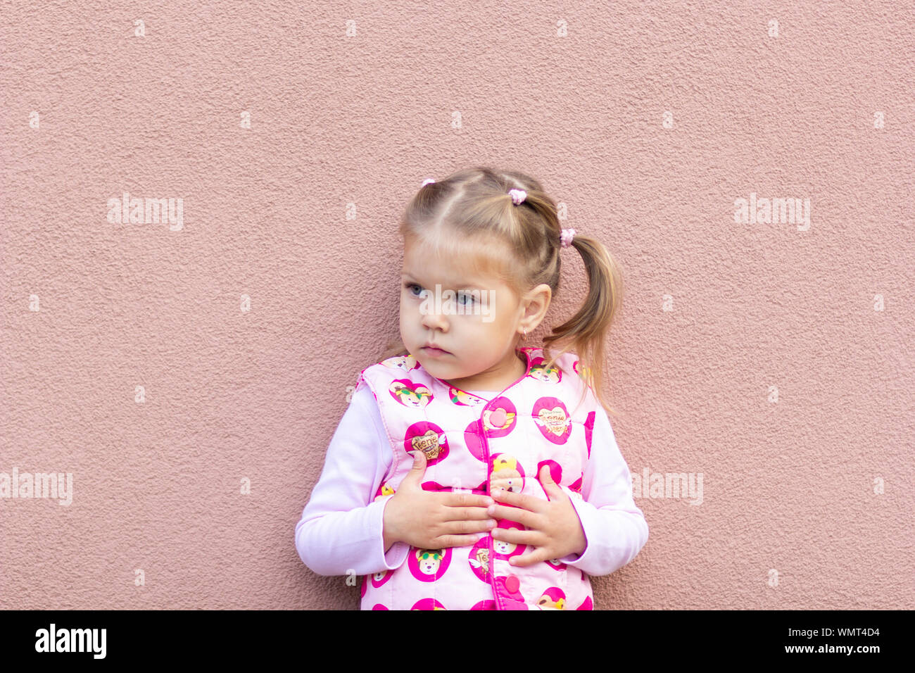 portrait of little girl without any emotions on pink background looking ...