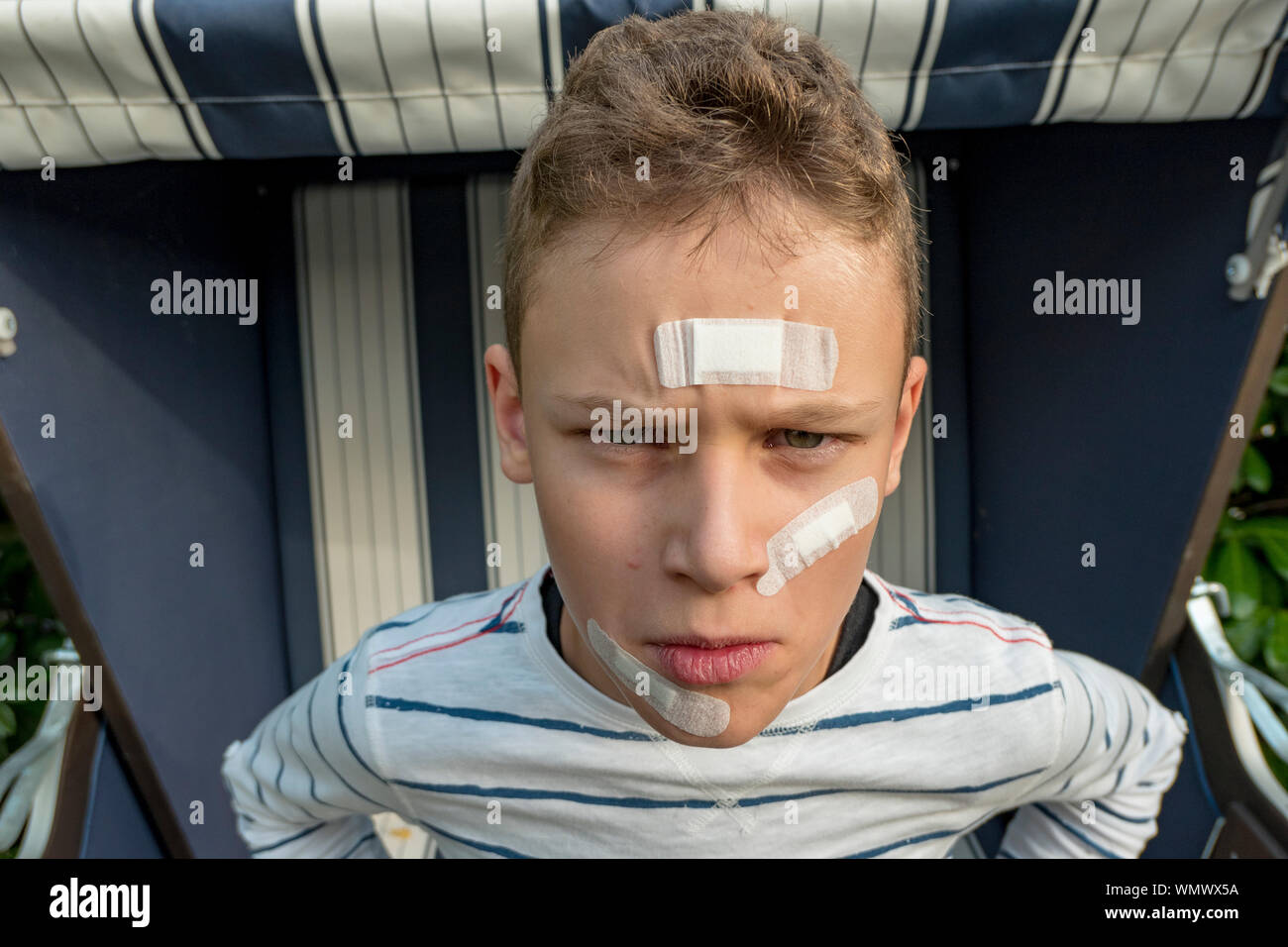 Boy with plaster on his face in front of a hedge laughing Stock Photo ...