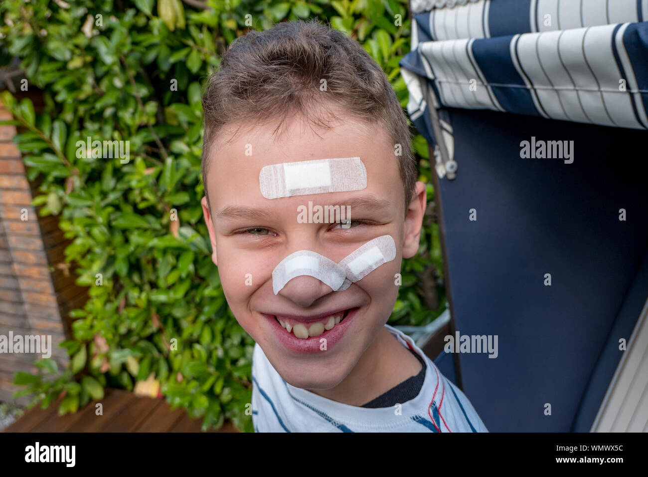 Boy with plaster on his face in front of a hedge laughing Stock Photo ...