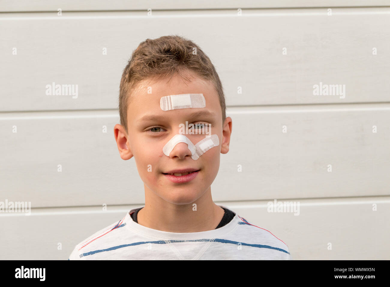 Boy with plaster on his face in front of a hedge laughing Stock Photo ...